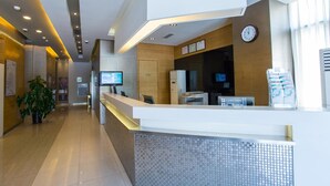 Uma área de recepção de hotel com design moderno, incluindo um balcão de atendimento, um relógio e uma tela digital.