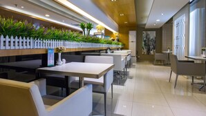 Interior moderno de restaurante com mesas e cadeiras brancas, teto de madeira e parede decorativa com plantas.