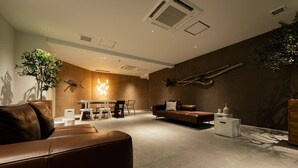 Uma sala de estar moderna com um sofá de couro marrom, uma área de jantar com cadeiras brancas e um galho de árvore decorativo na parede.