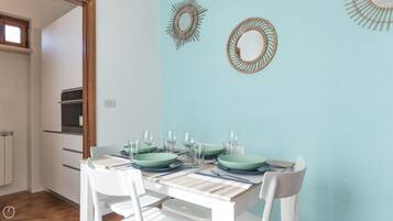 Uma sala de jantar com mesa posta para quatro pessoas, cadeiras brancas e duas decorações nas paredes.