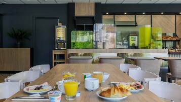 Uma mesa de madeira com cadeiras brancas e uma variedade de itens para o café da manhã, incluindo croissants, frutas e suco de laranja.