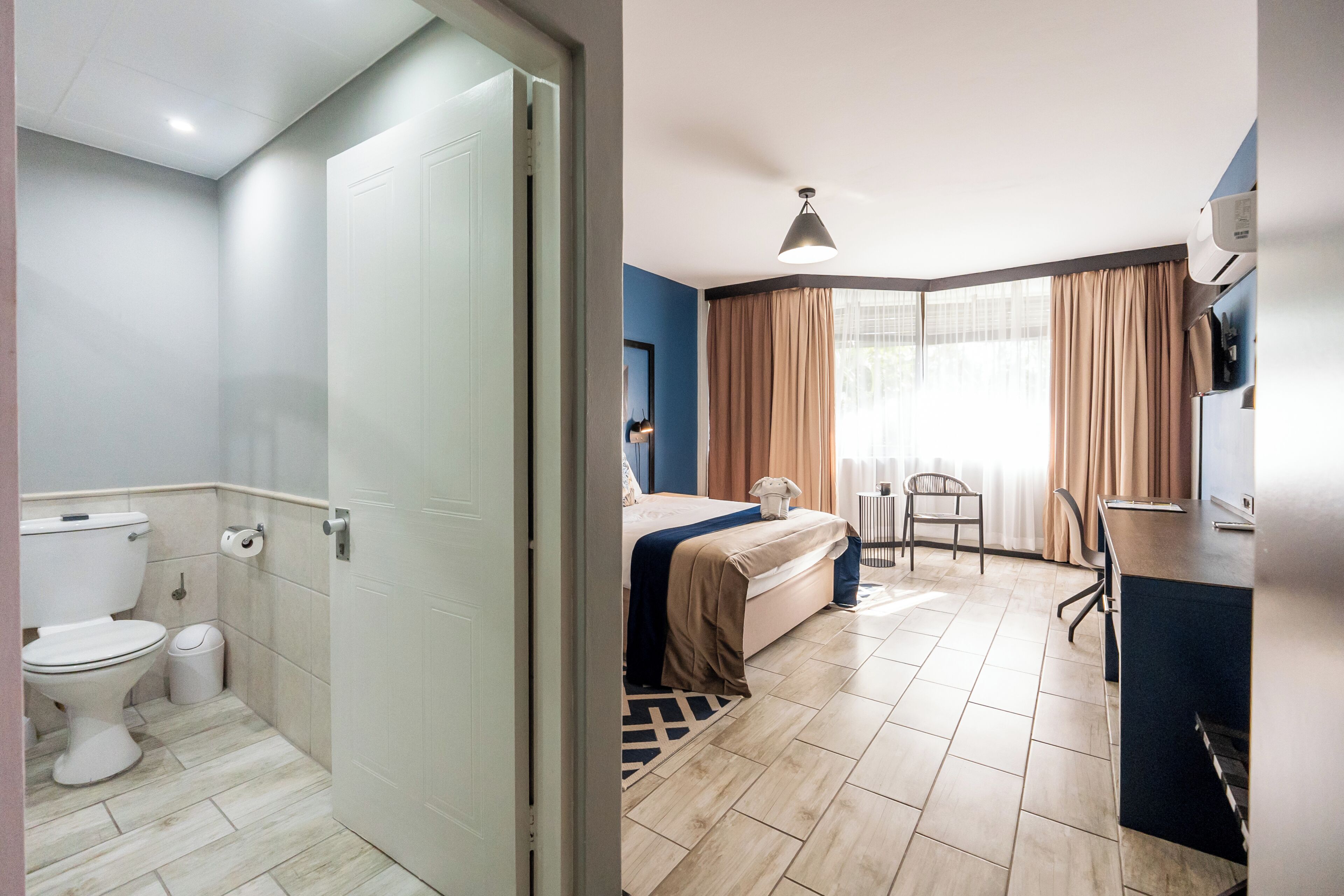 Quarto de hotel com banheiro, cama, escrivaninha e cadeira.