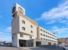 Um hotel tipo bed and breakfast com design moderno, destacando uma placa visível, várias janelas e um estacionamento.