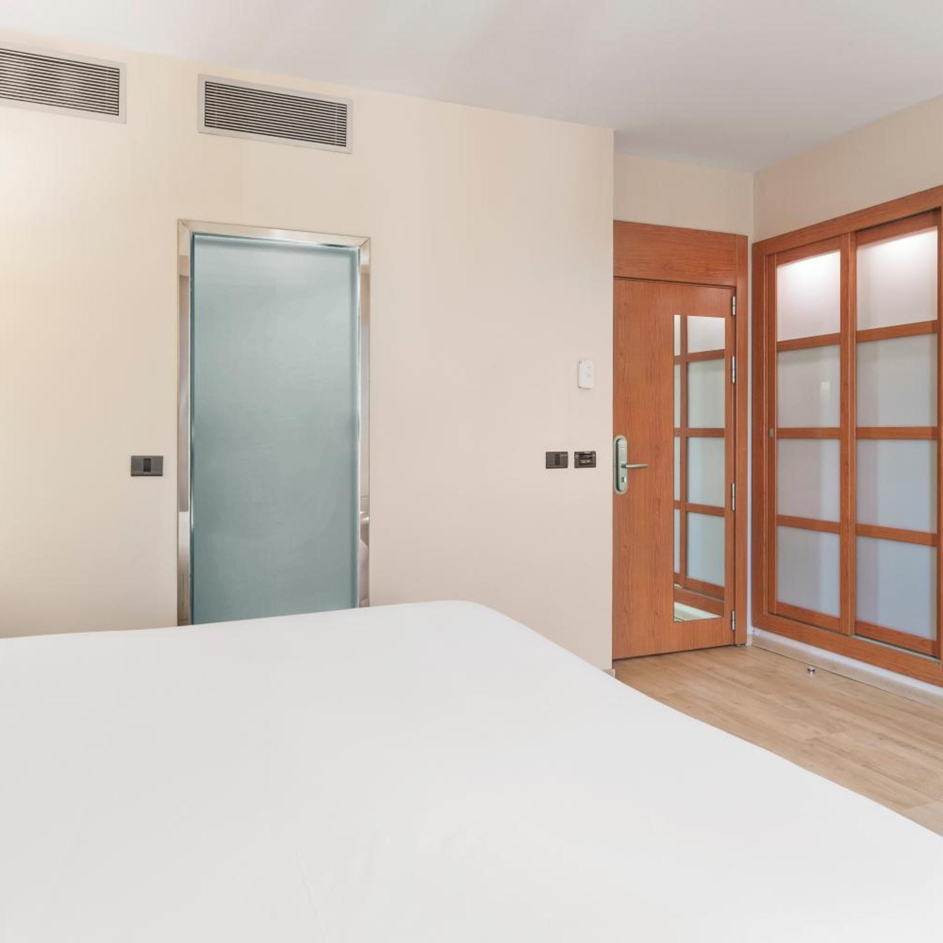 Quarto com cama, porta e guarda-roupa com painéis de vidro jateado.