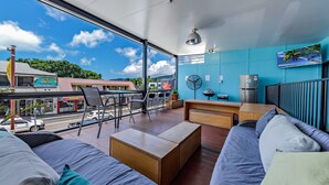 Quarto moderno com uma janela grande, um sofá, uma mesa de centro de madeira, uma mesinha e uma TV fixada na parede.