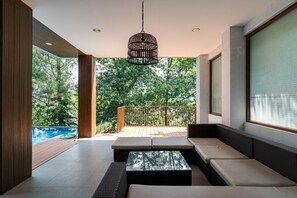 Uma área de estar moderna ao ar livre, vista para a piscina, deck de madeira e luminária pendente.