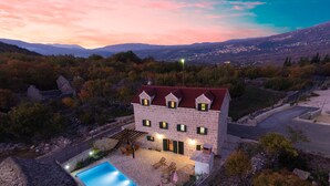 Uma casa de pedra com piscina, rodeada por árvores e colinas.