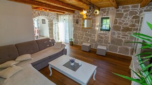 Uma sala de estar acolhedora com parede de pedra, teto de madeira, um sofá, uma mesa de centro e uma pequena mesa lateral.