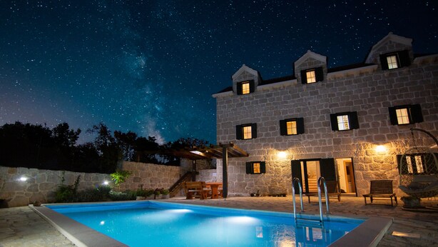 Edifício de pedra com piscina à noite, iluminado por iluminação ambiente.