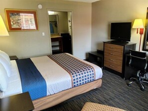 Quarto de hotel com cama, escrivaninha, cadeira, televisão e espelho.