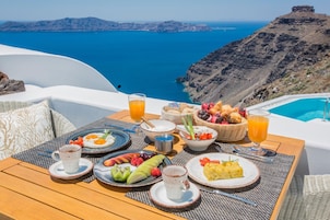 Mesa de café da manhã com ovos, torradas, frutas e suco, com vista para o oceano.