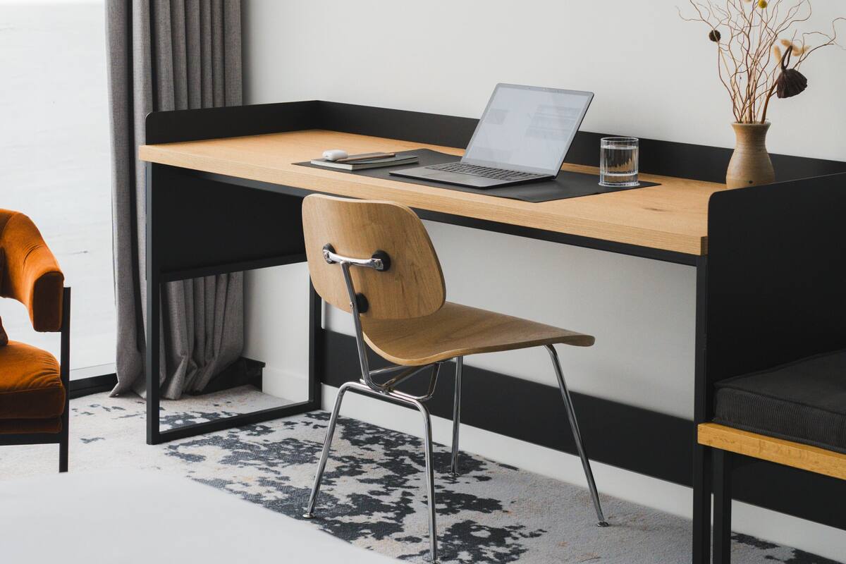 Um espaço de trabalho moderno com uma mesa de madeira, um laptop, uma cadeira e um vaso com ramos secos.