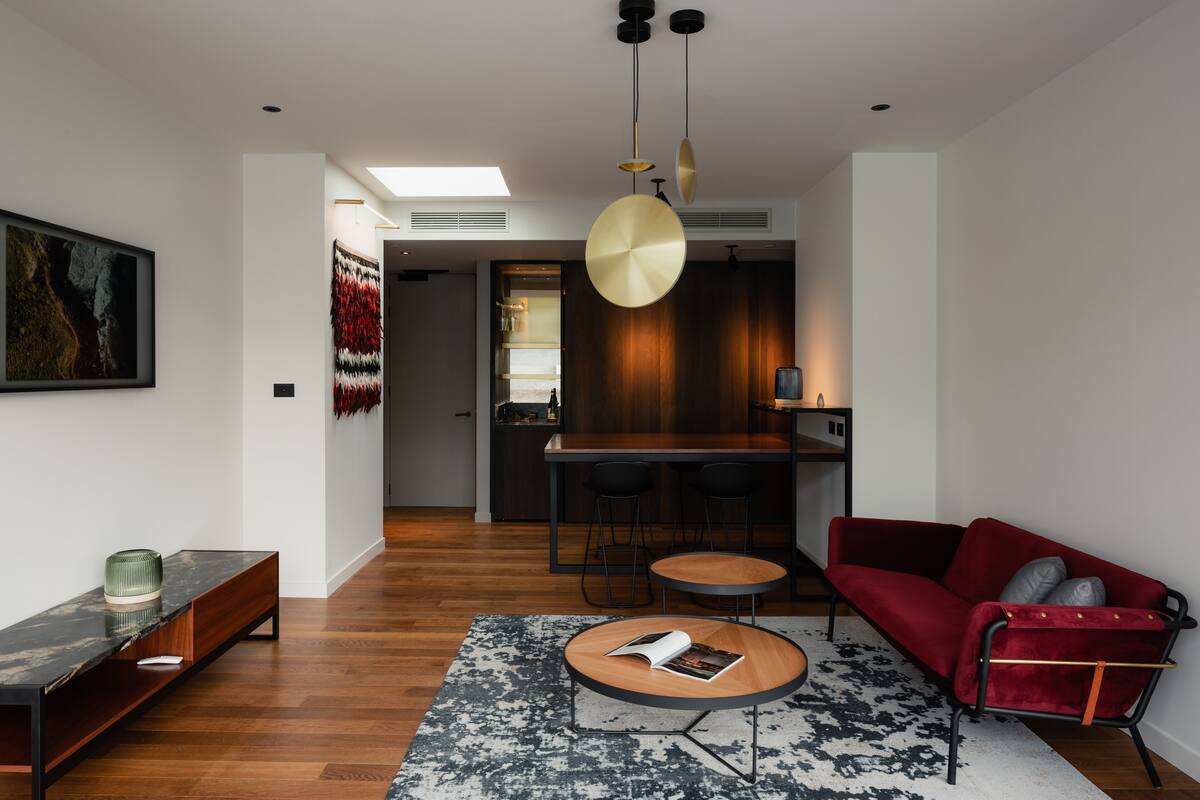 Uma sala de estar moderna, com um sofá vermelho, uma mesa de centro e uma área de jantar com cozinha ao fundo.