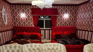Um quarto luxuoso com uma cama grande, duas poltronas vermelhas estofadas, um sofá branco e um candelabro.