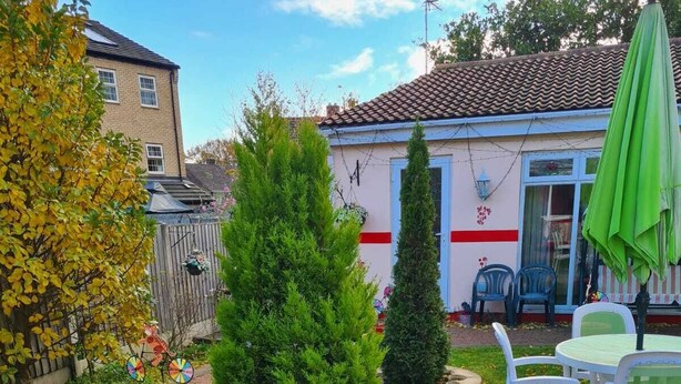 Um jardim com uma estátua de pavão, uma pequena árvore e um espaço de varanda com cadeiras e uma mesa.