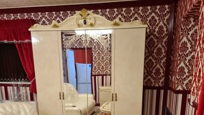 Quarto com um sofá de couro branco, um guarda-roupa branco com espelho e um tapete estampado.
