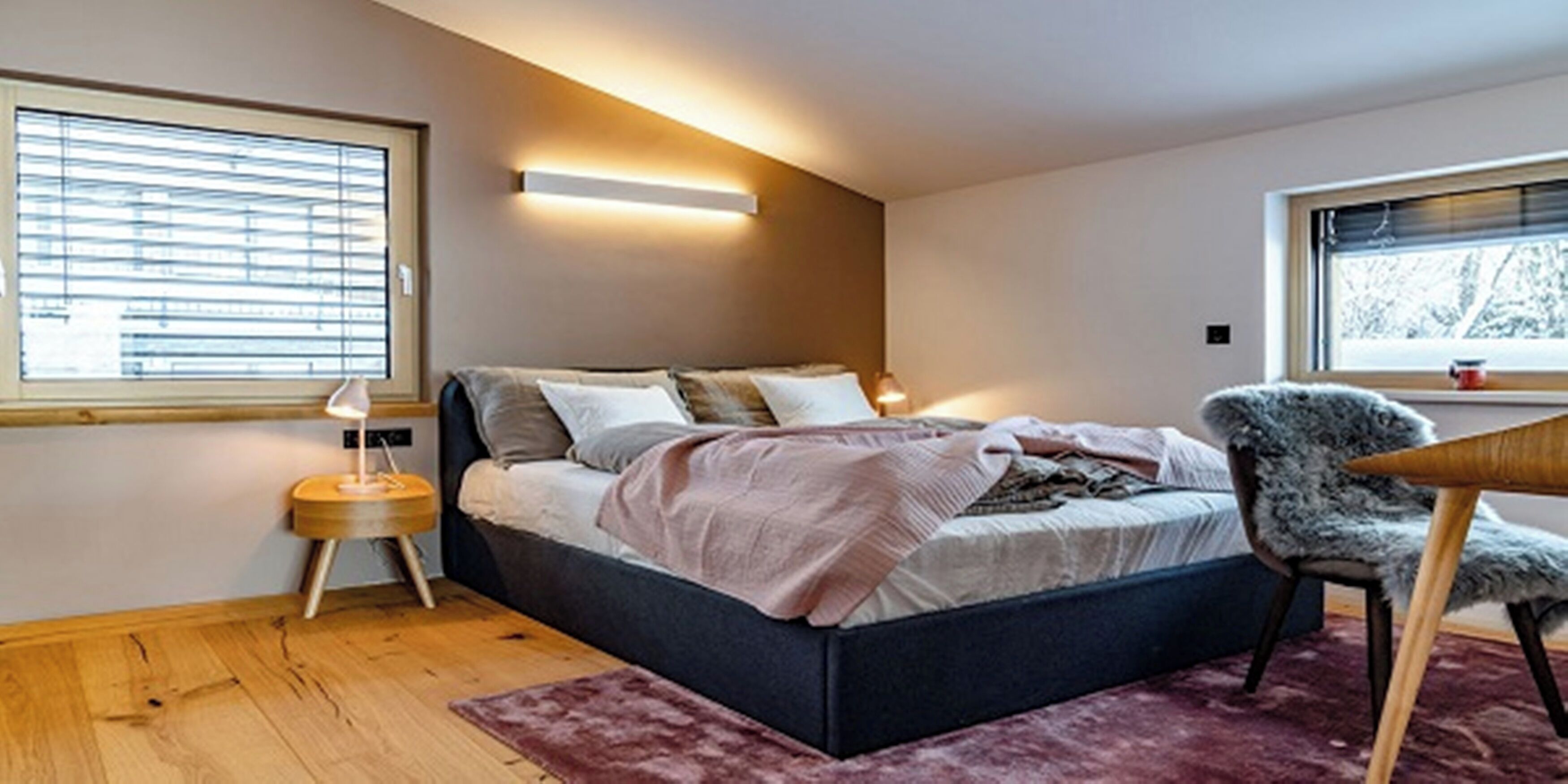 Quarto com cama, luminária de cabeceira, cadeira e janela com persianas.