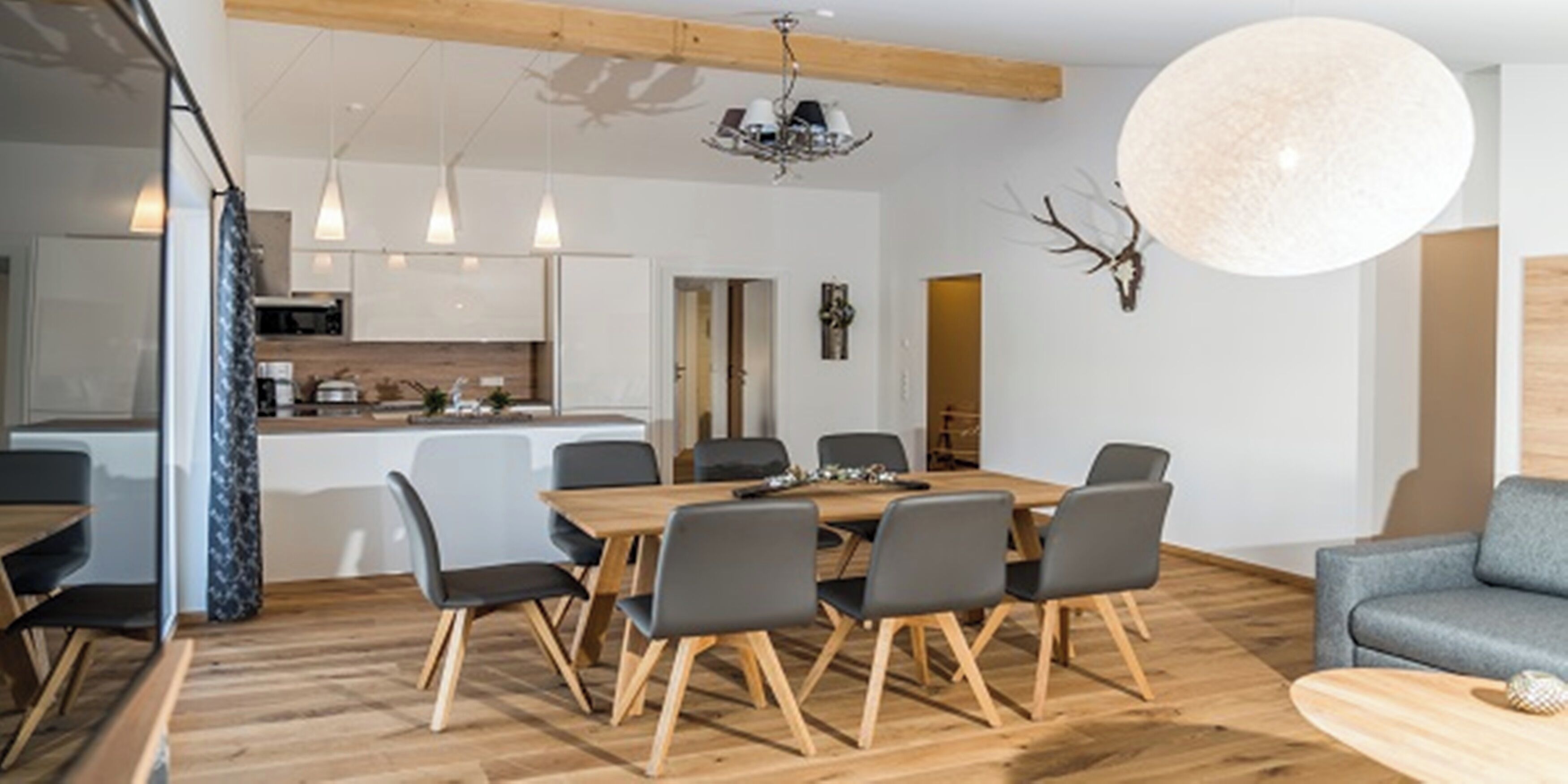 Uma sala de jantar moderna com uma mesa e cadeiras de madeira, um candelabro e um chifre de veado pendurado na parede.