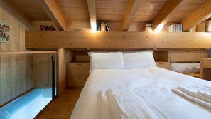 Um quarto com teto de madeira, uma cama com roupa de cama branca e uma mesa de cabeceira.