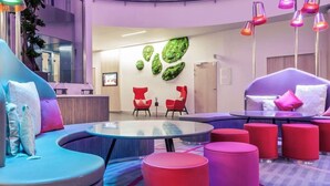 Uma área de estar moderna com uma mesa redonda de vidro, assentos em vermelho e azul, e arte verde nas paredes.