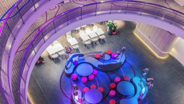 Um espaço interno moderno com área de estar circular, uma passarela coberta e mesas com cadeiras.