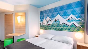 Quarto de hotel com uma cama, um banquinho verde, uma mesa de cabeceira de madeira e uma parede com um desenho geométrico de montanhas.