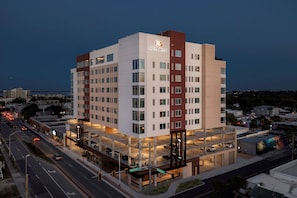 Um hotel com vários andares, um letreiro chamativo do 'Hotel Melby', uma garagem de estacionamento e vista da rua com trânsito.