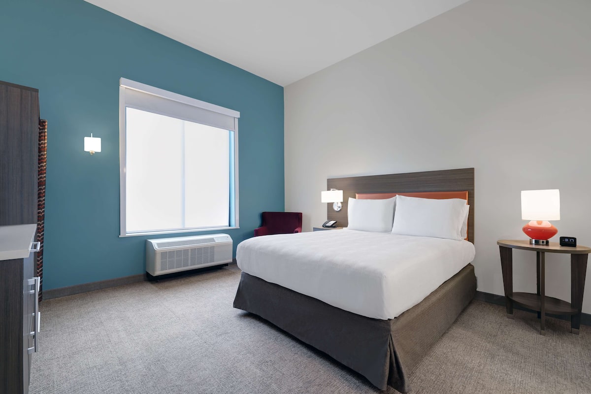 Quarto de hotel com uma cama grande, janela, aquecedor, escrivaninha e luminária.