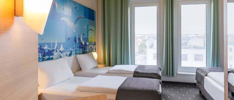 Quarto de hotel com cama, sofá, escrivaninha e uma janela grande com cortinas.