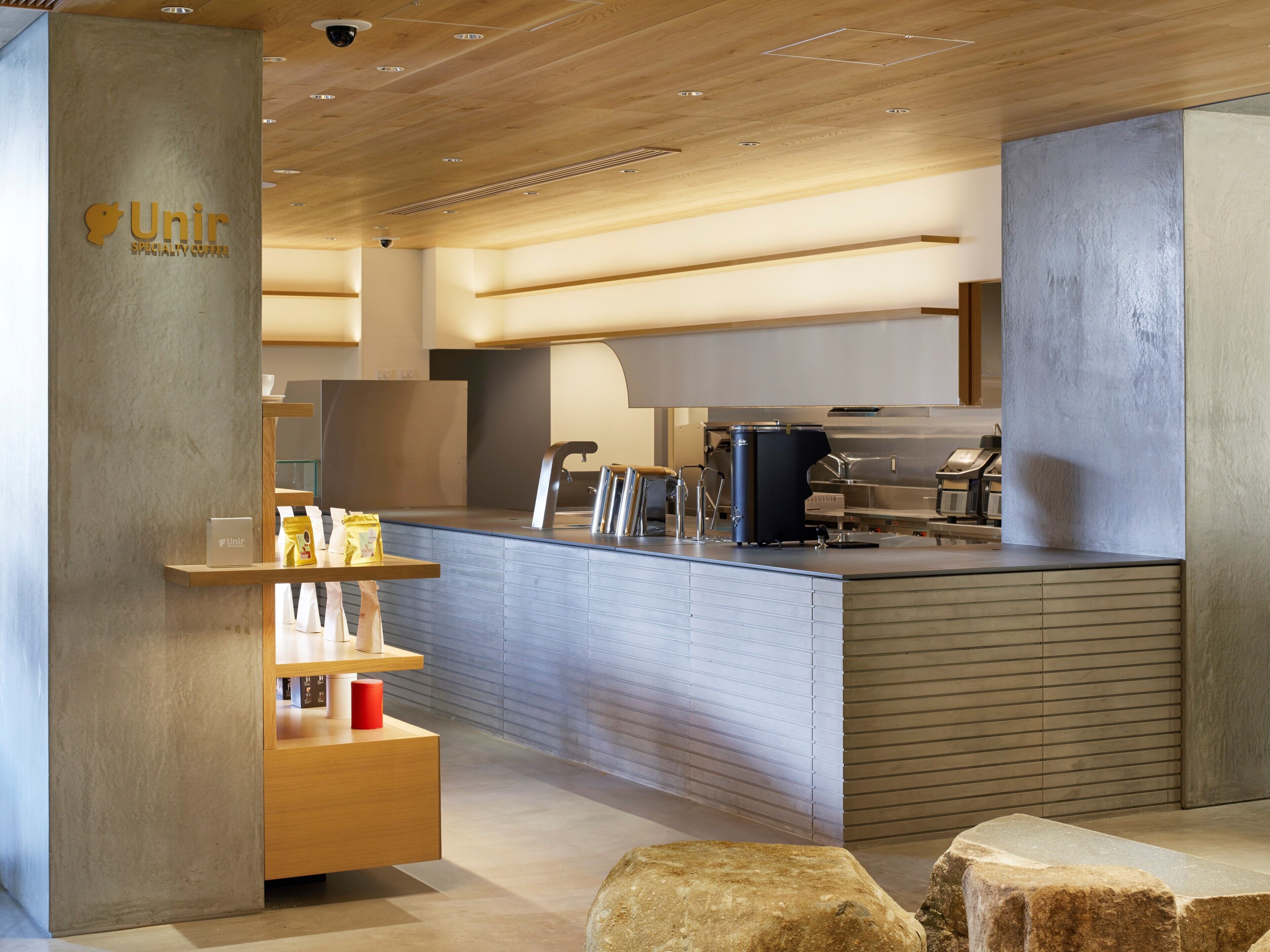 Interior de cafeteria moderna com balcão de madeira, máquina de café e área de estar com banquetas.