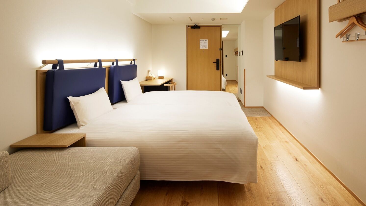 Quarto de hotel com uma cama grande, mesas de cabeceira, televisão na parede e piso de madeira.