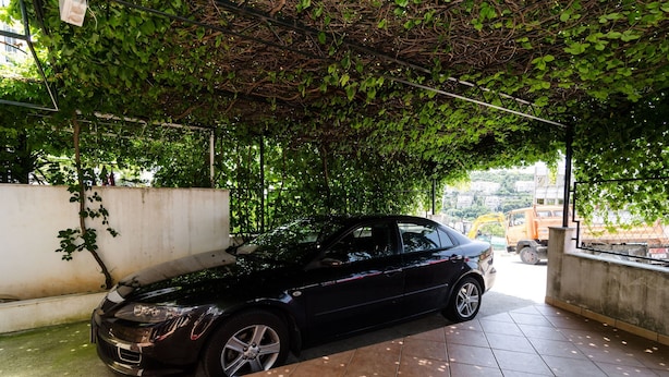 Um carro preto estacionado sob uma cobertura com piso de azulejos e parede de concreto.