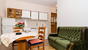 Um espaço compacto com mesa de jantar, cadeiras, sofá verde e uma pequena cozinha equipada.