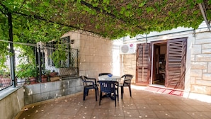 Um p átio externo com uma mesa e cadeiras, rodeado por um muro de pedra e coberto por uma trepadeira folhosa.