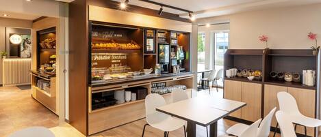 Um café moderno com um balcão exibindo comida e bebidas, cadeiras brancas ao redor de uma mesa, e vista para o exterior.