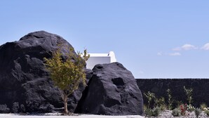 Um edifício moderno com fachada branca, integrado entre grandes rochas escuras, sob um céu azul límpido.