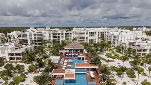 Resort com vários edifícios brancos, área de piscina central com espreguiçadeiras e palmeiras.