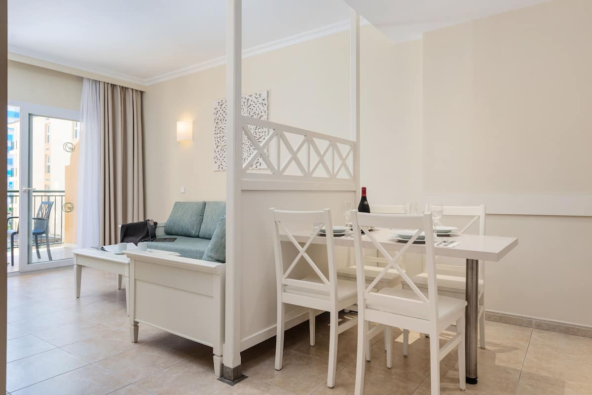 Uma sala de estar moderna e minimalista, com um sofá branco, uma mesa de jantar com cadeiras brancas e uma porta de vidro que dá para uma área externa.