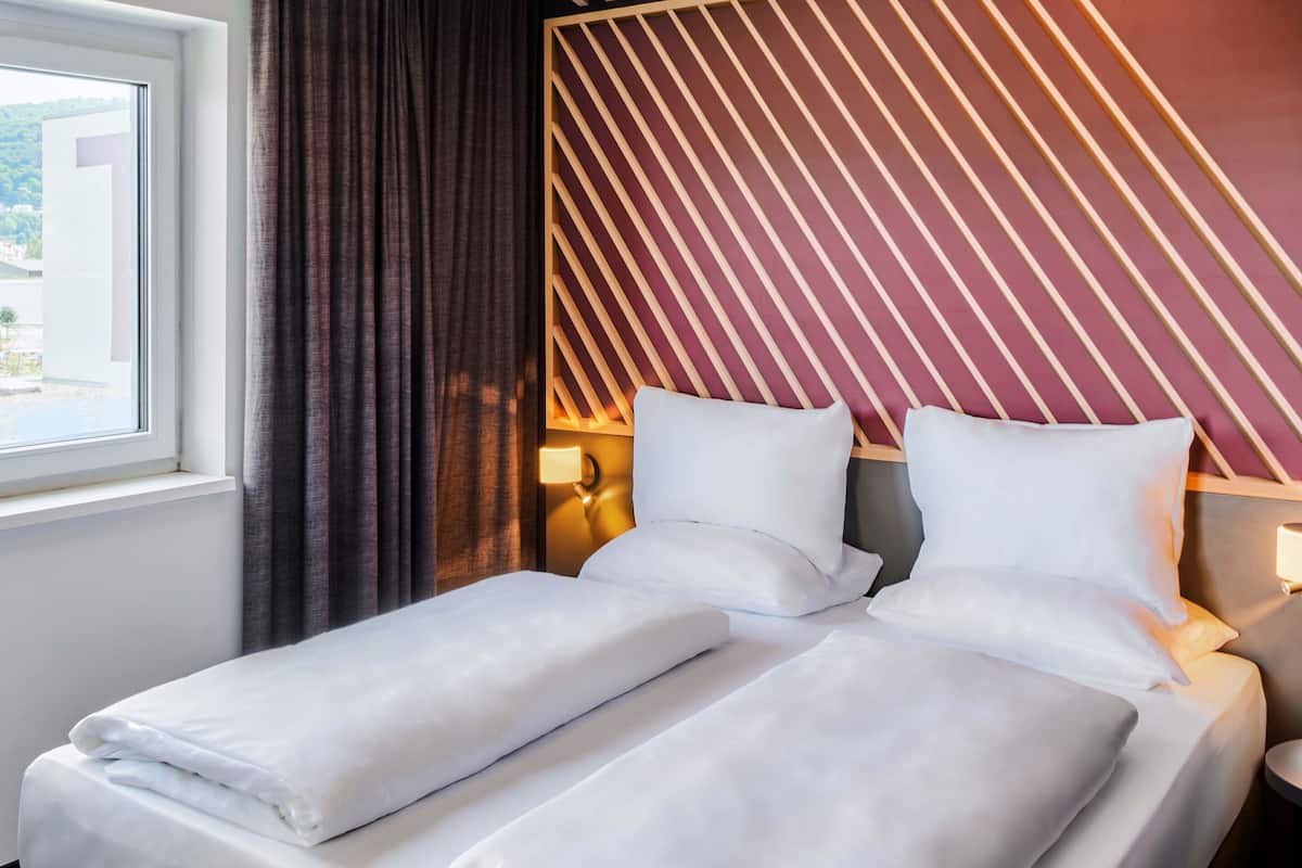 Quarto de hotel com cama, janela e parede com padrão listrado.