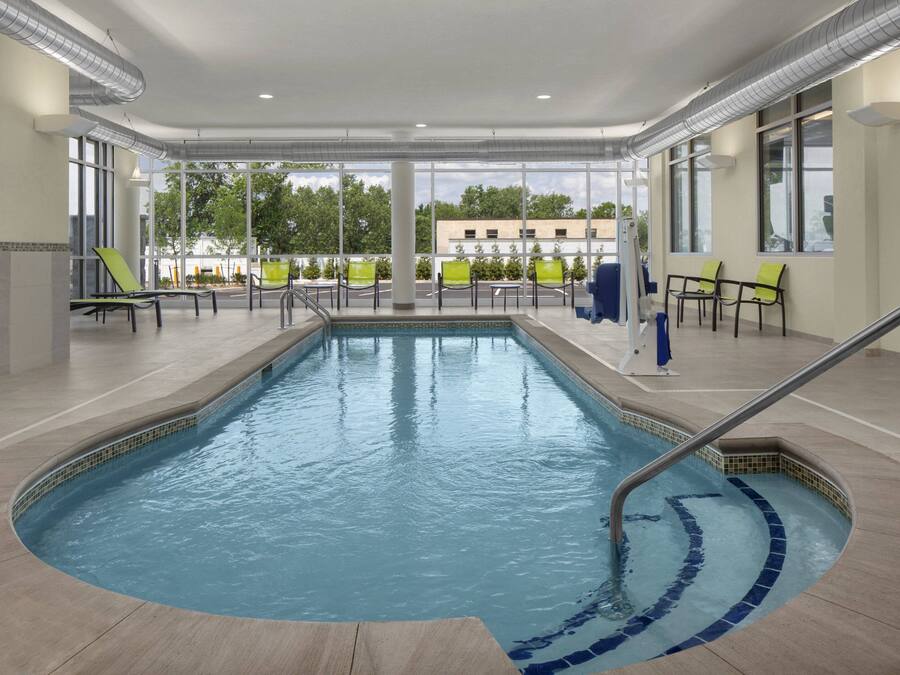 Piscina interior com paredes de vidro transparente, borda em azulejo e escada de acesso.