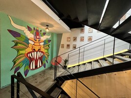 Uma escadaria com um mural colorido na parede, uma luminária no teto e quadros enquadrados na parede.