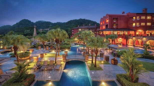 Um resort com piscina, palmeiras e uma ponte.
