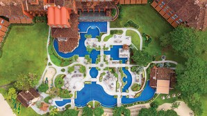 Vista aérea de um resort com várias piscinas, jardins bem cuidados e diversas áreas de estar ao ar livre.