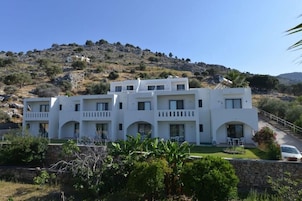 Um edifício branco de vários andares com varandas, com uma paisagem montanhosa ao fundo.