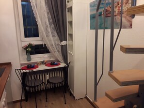 Uma pequena área de refeições com uma mesa, cadeiras, um radiador, uma janela com cortinas e um quadro na parede.