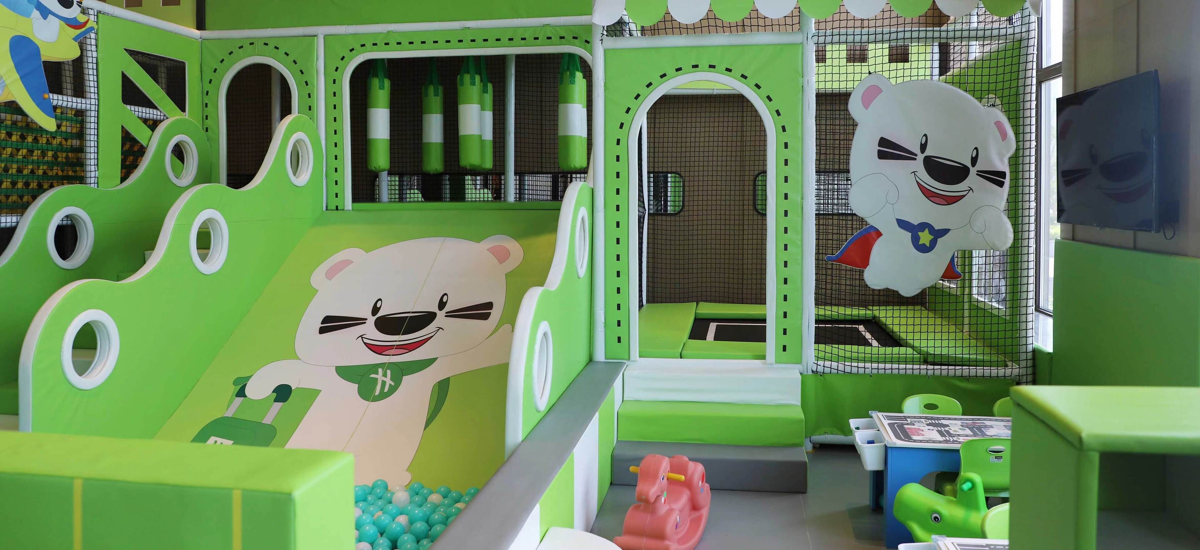 Espaço de recreação infantil com paredes verdes, uma decoração de urso e um trampolim.