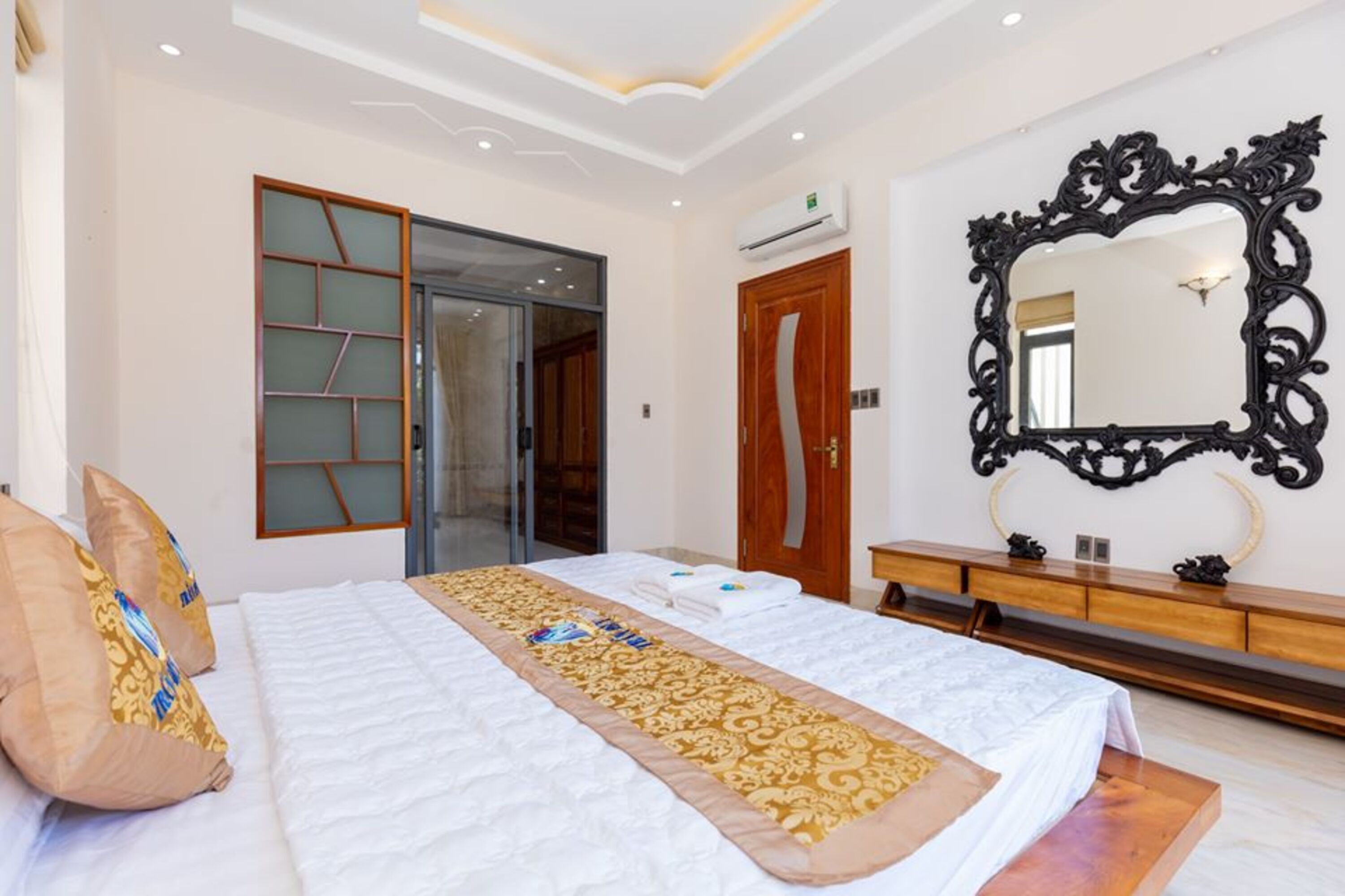 Quarto de hotel com uma cama grande, cómoda de madeira, espelho e porta de correr para um banheiro.