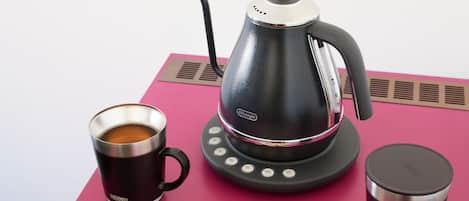 Uma cafeteira com uma chávena de café sobre uma mesa rosa.