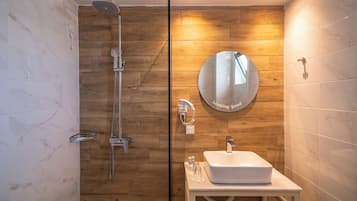 Casa de banho moderna com divisória de vidro, lavatório branco, espelho e chuveiro.