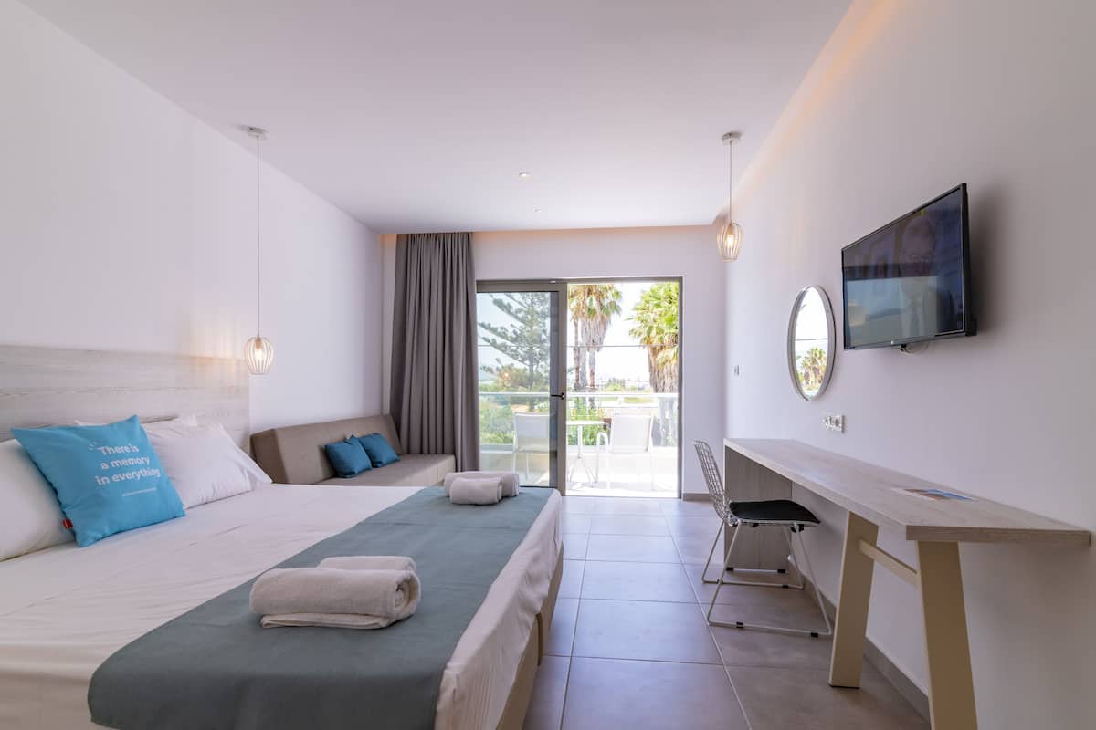 Quarto de hotel moderno com cama, escrivaninha, televisão e varanda com área de estar ao ar livre.